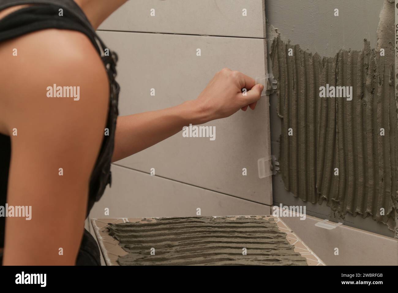 Woman tiling bathroom walls, applying adhesive on a tile and placing ...