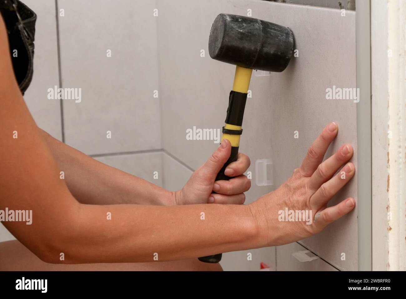Woman tiling bathroom walls, pressing tile into a glue with rubber ...