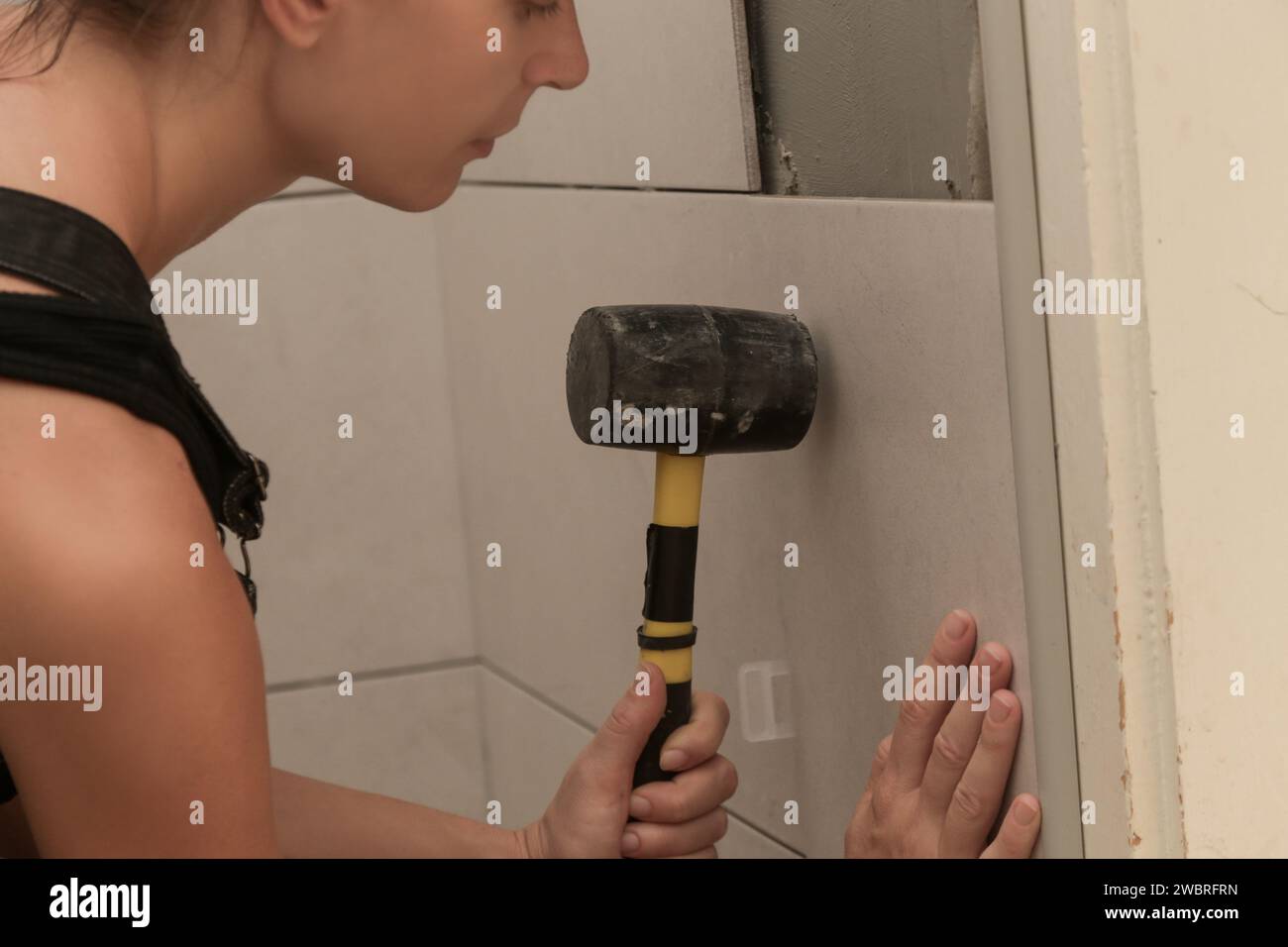 Woman tiling bathroom walls, pressing tile into a glue with rubber ...