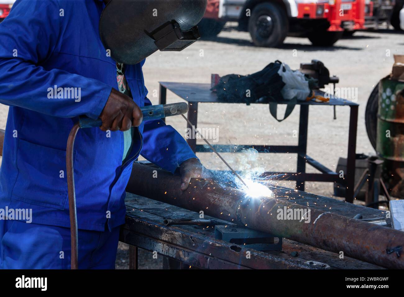 african welder outdoors welding a broken pipe, truck in the background ...
