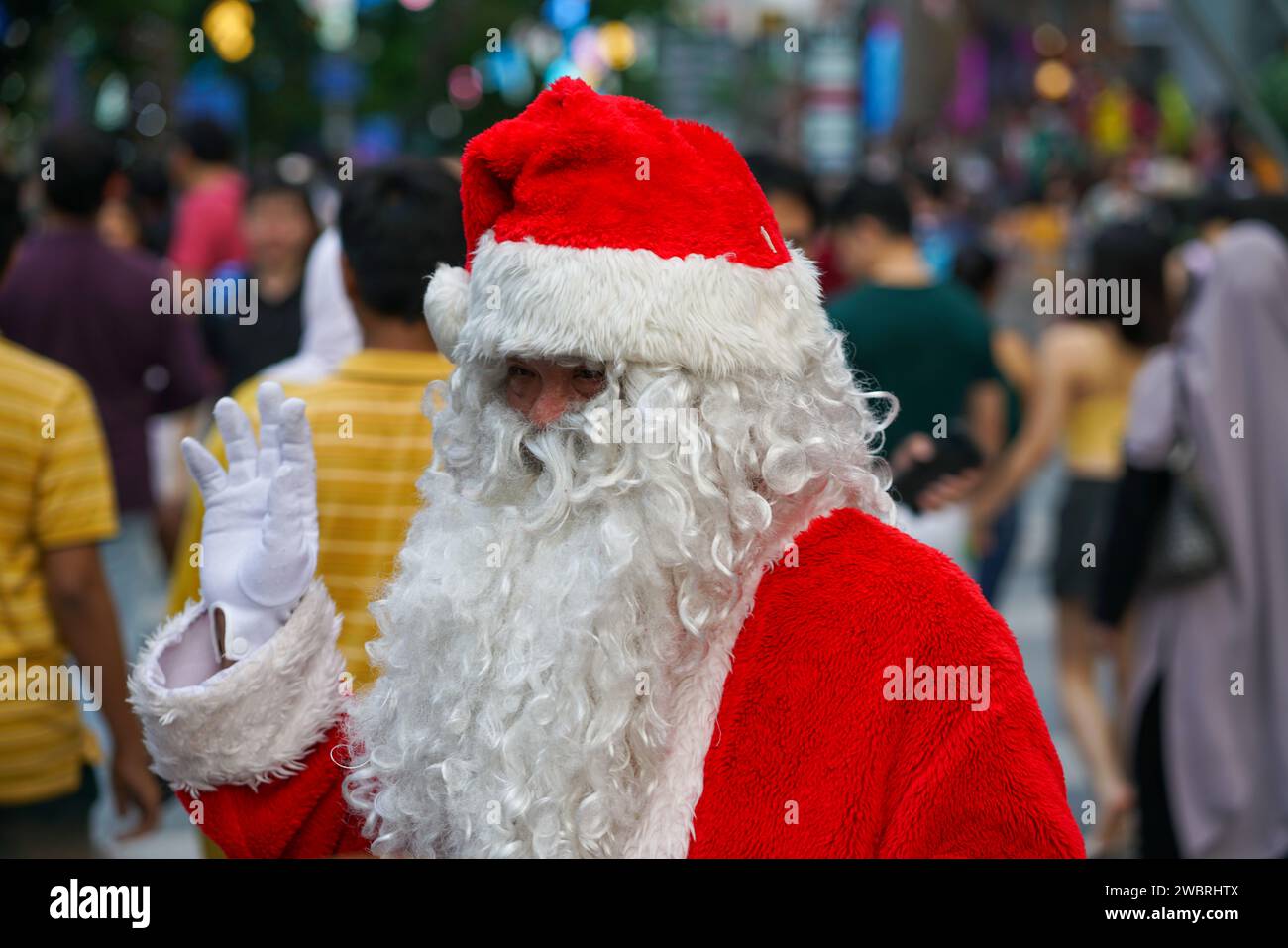 A festive man dressed as Santa Claus stands on a busy street waving ...