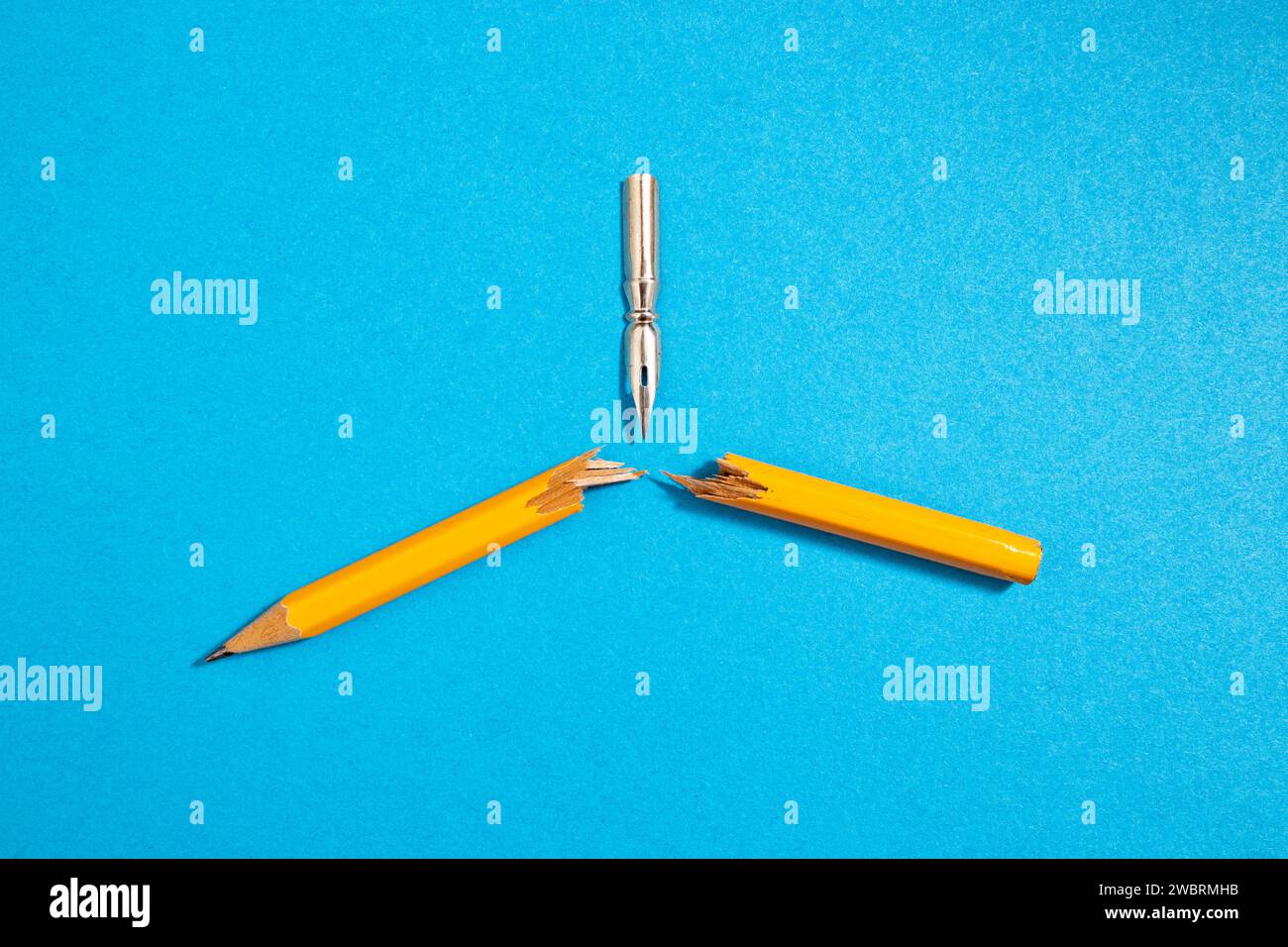 Vintage pen nib breaking a crayon in half, on blue paper background ...