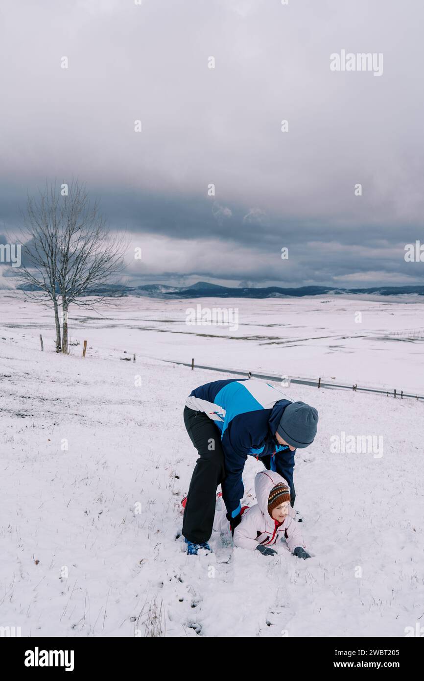 Dad leaned over the little girl lying on her stomach in the snow and ...