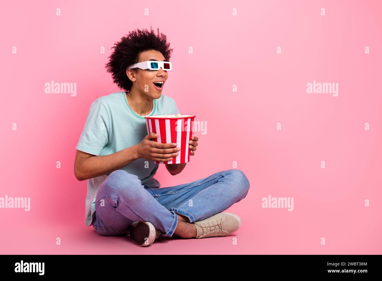 Full length photo of handsome young male sit floor enjoy movie eat ...