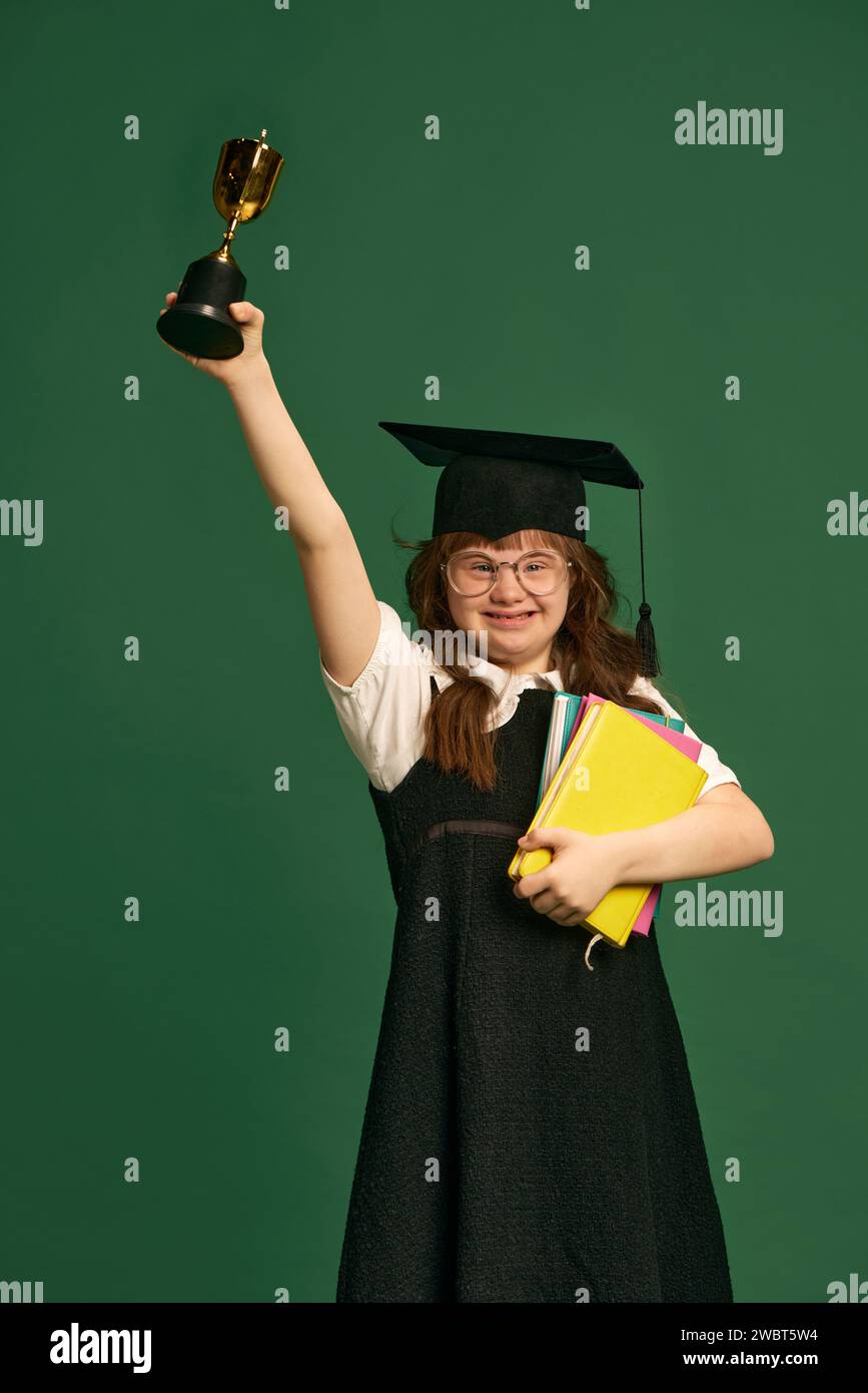 Happy girl with down syndrome standing in graduation cap, books and ...