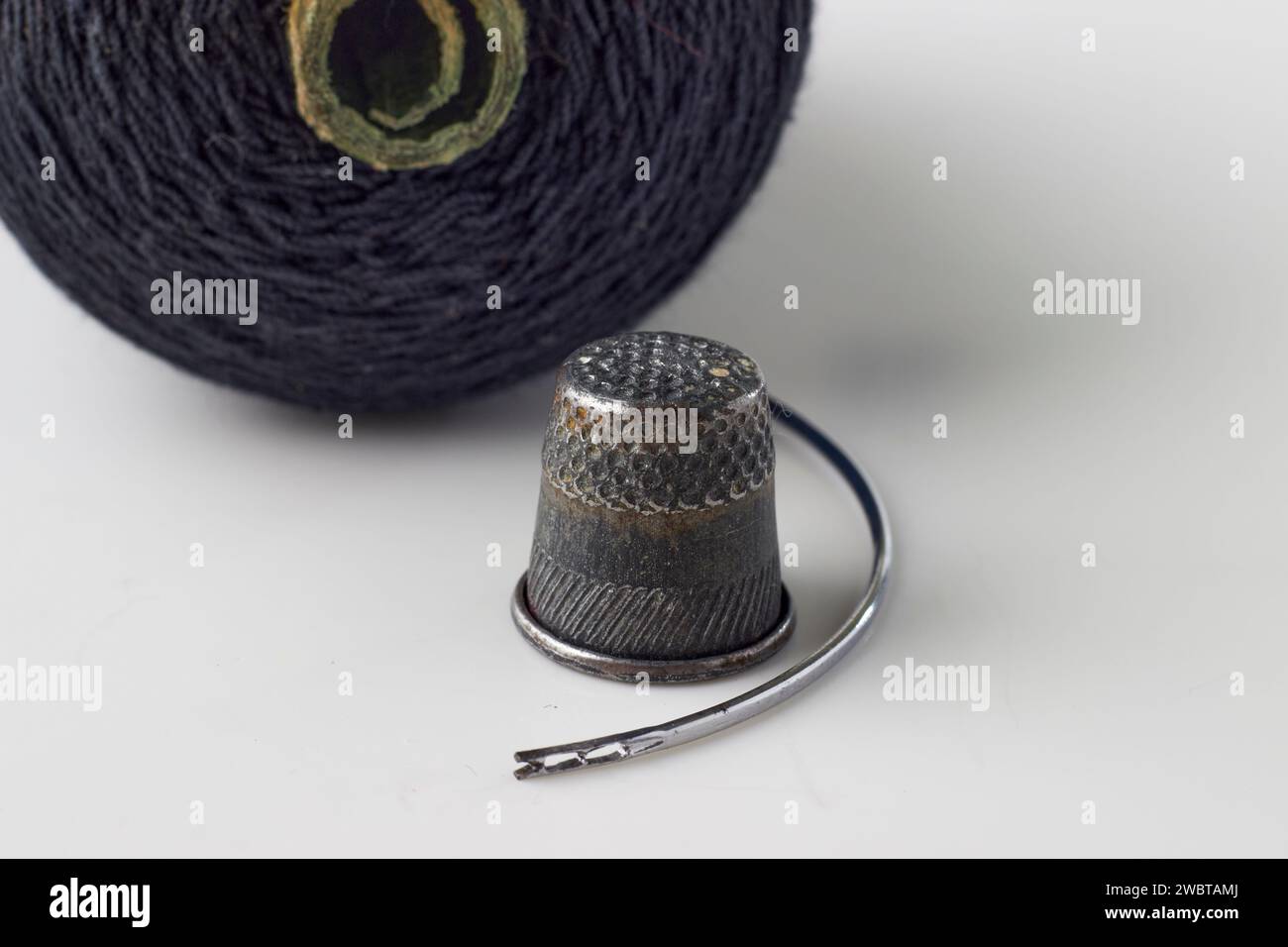 Metal thimble, sewing needle and spool of black thread on a white ...