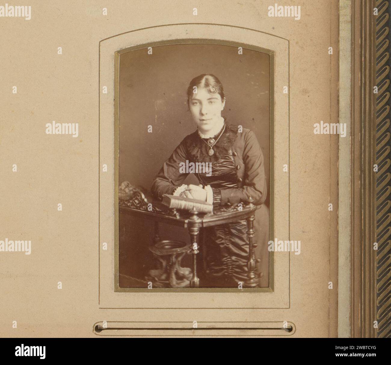 Portrait of a standing young woman, leaning on a table with book ...