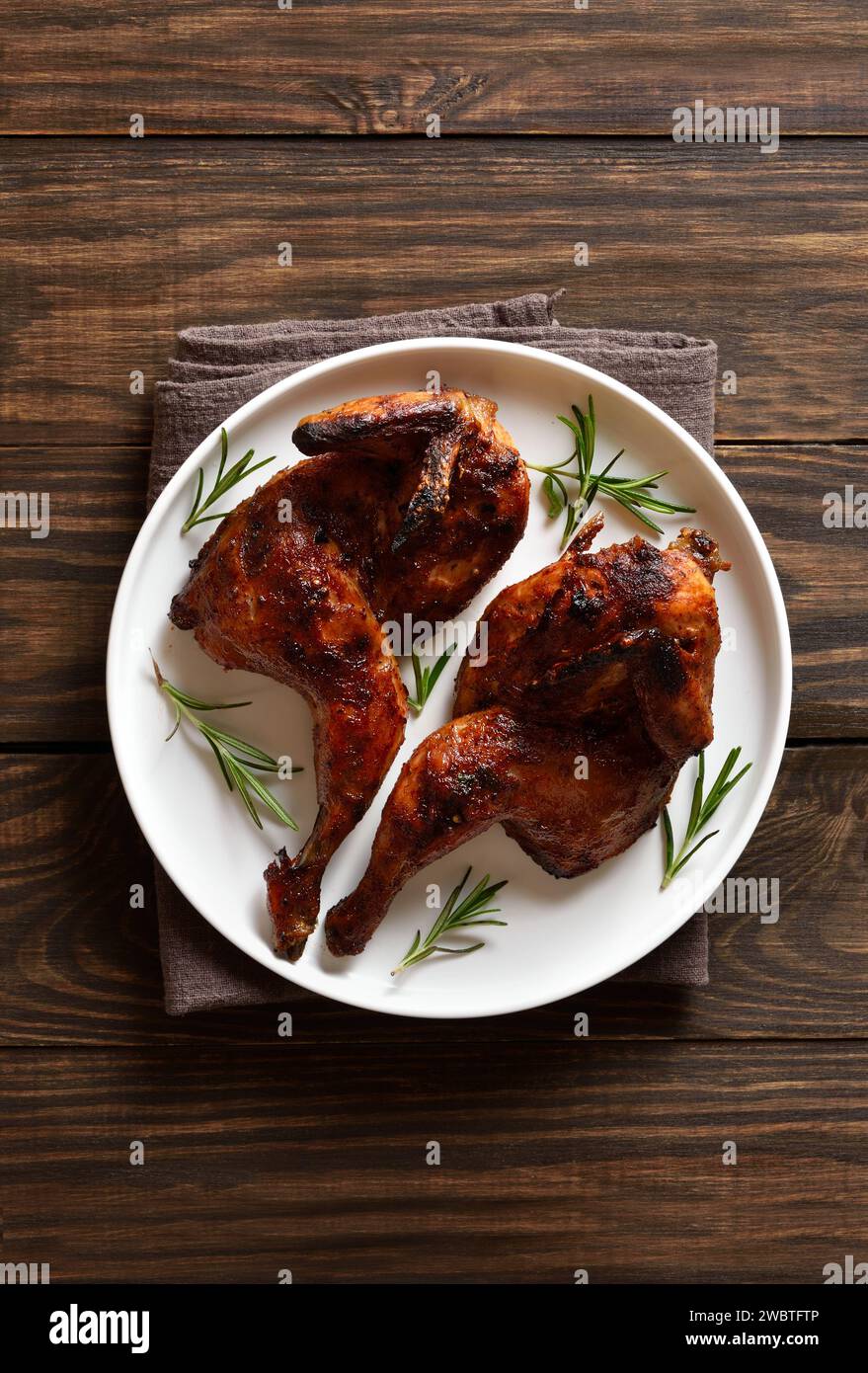 Roasted half chicken with rosemary on white plate over wooden ...