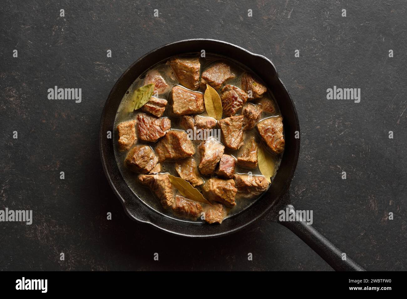 Braised beef in cast iron skillet over dark stone background. Beef ...