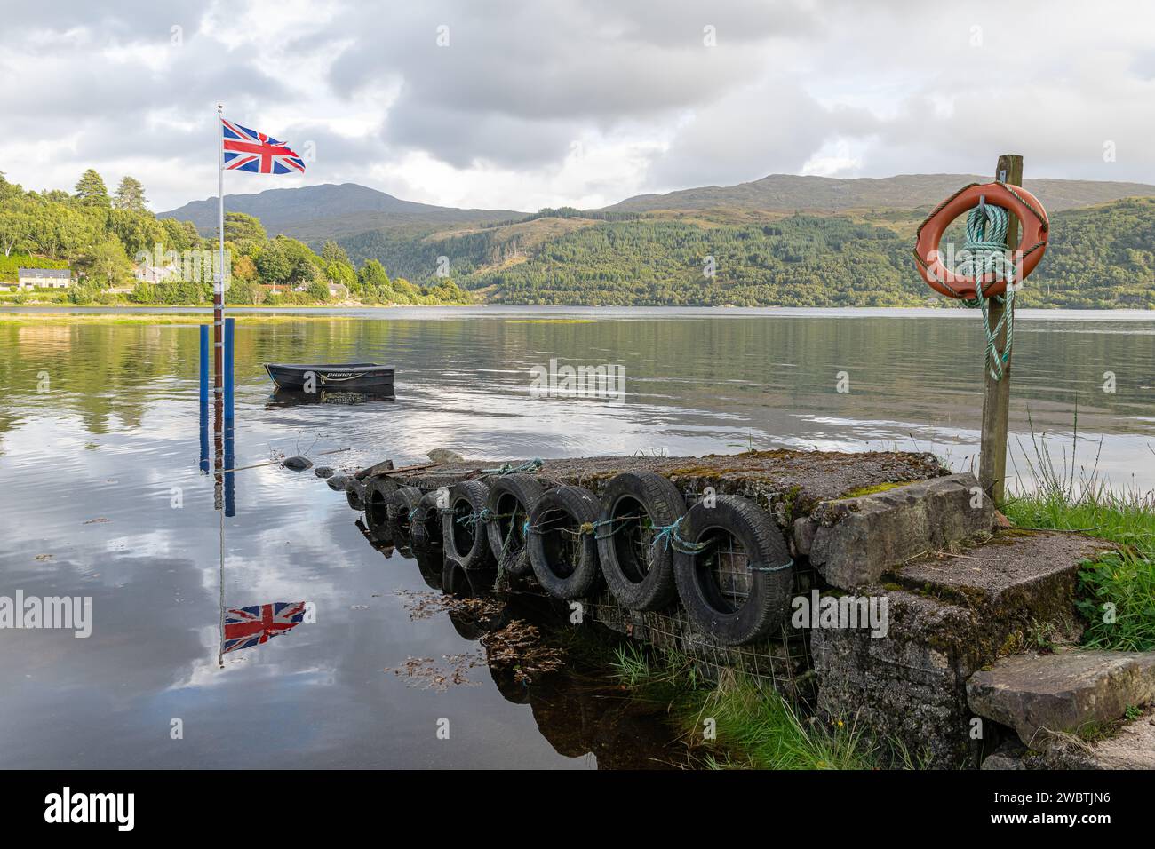 Union Jack flag on a pole with a boat tied up at high tide in sea Loch ...