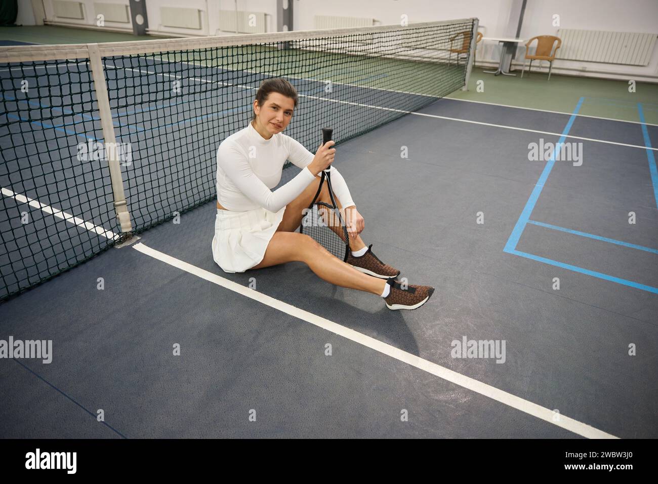 Woman tennis player with racket in hands looking at camera sitting on ...