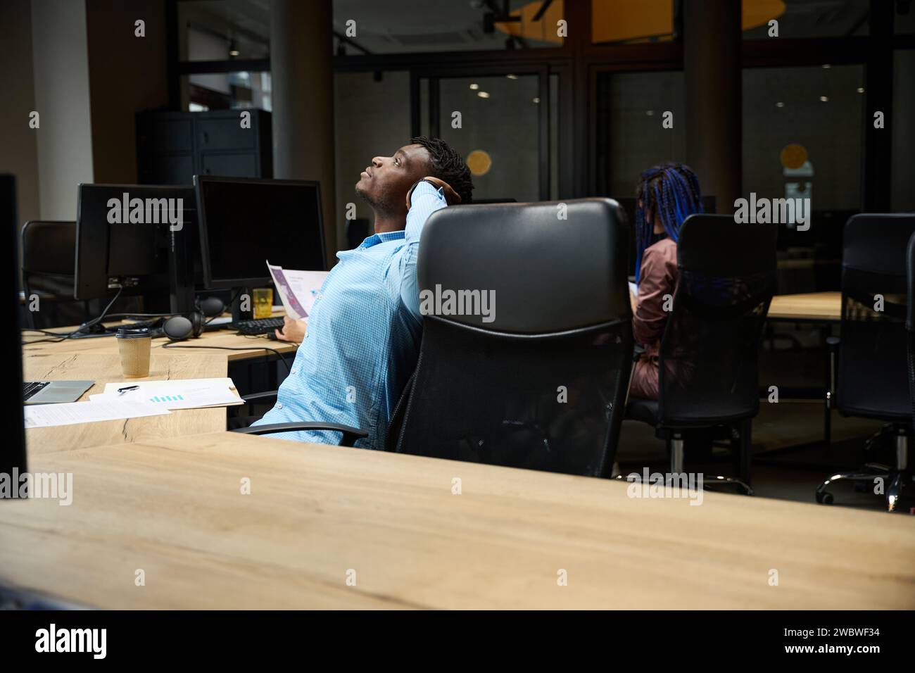 Tired African American office worker taking a break leaning on chair ...