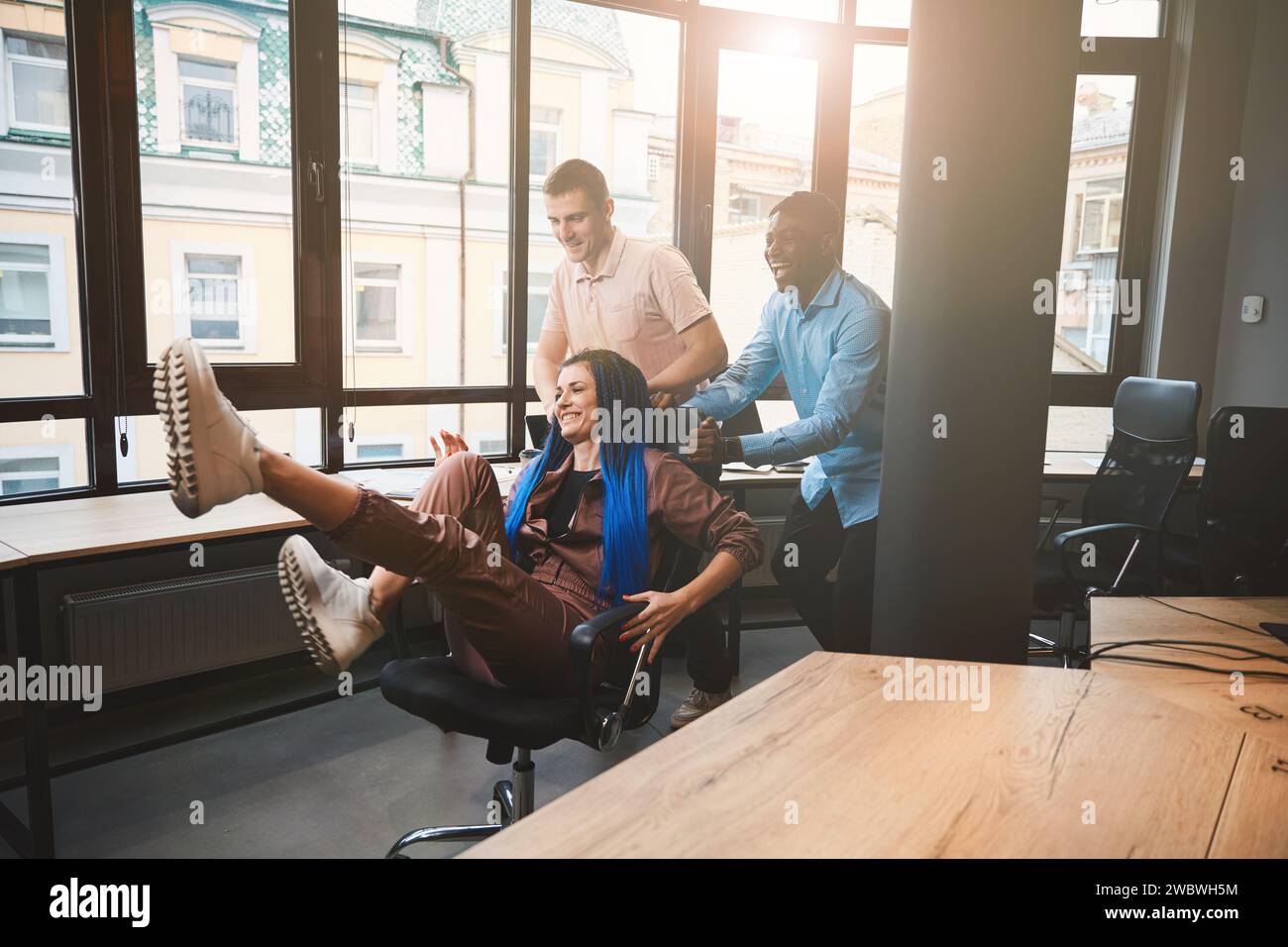 Male colleagues having fun rolling female colleague in wheeled armchair ...