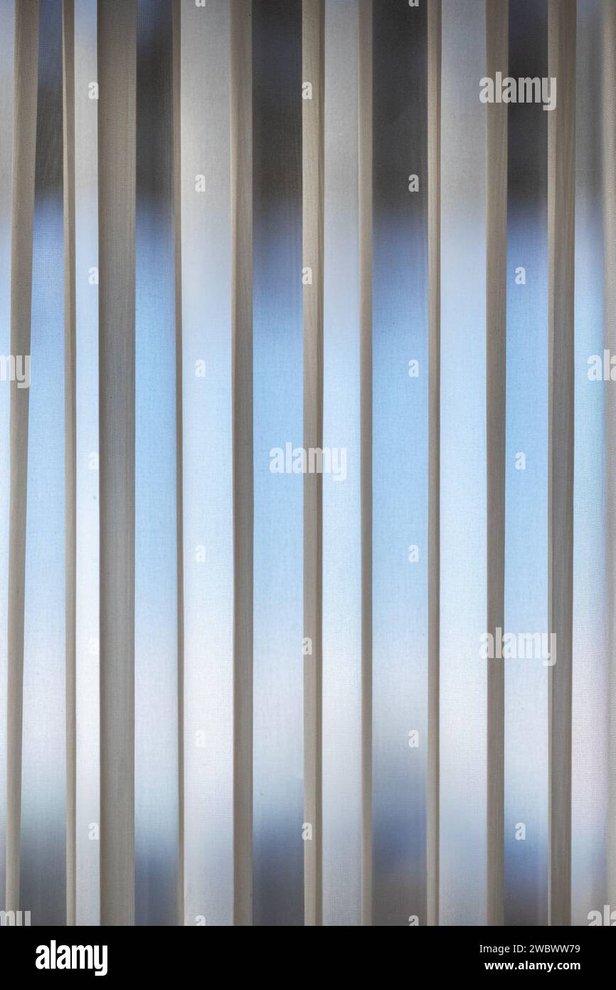 Filmy, sheer white curtains hang in folds in front of a window ...