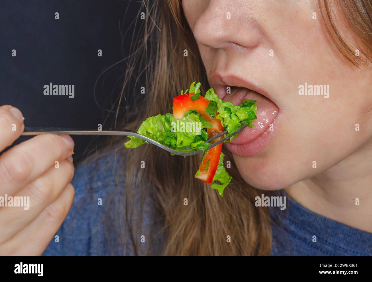 Salad on fork in a woman's mouth. Part of the face of a woman eating a ...