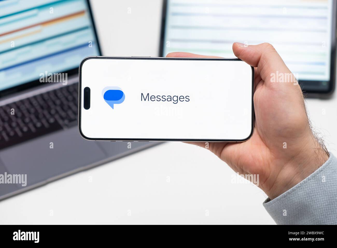 Messages logo of app on the screen of mobile phone held by man in front ...