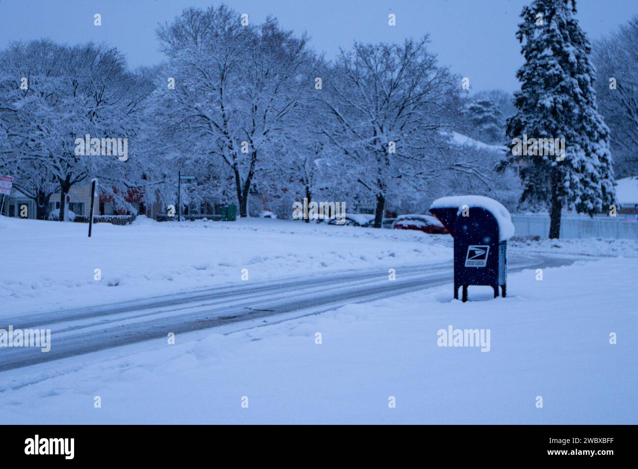 A bright blue mailbox stands tall on the side of a quiet road, ready to ...