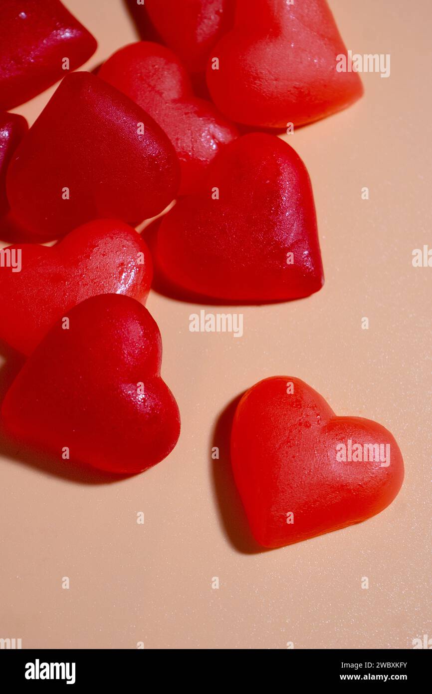 Red heart-shaped candies resting on a pastel orange surface, one of ...