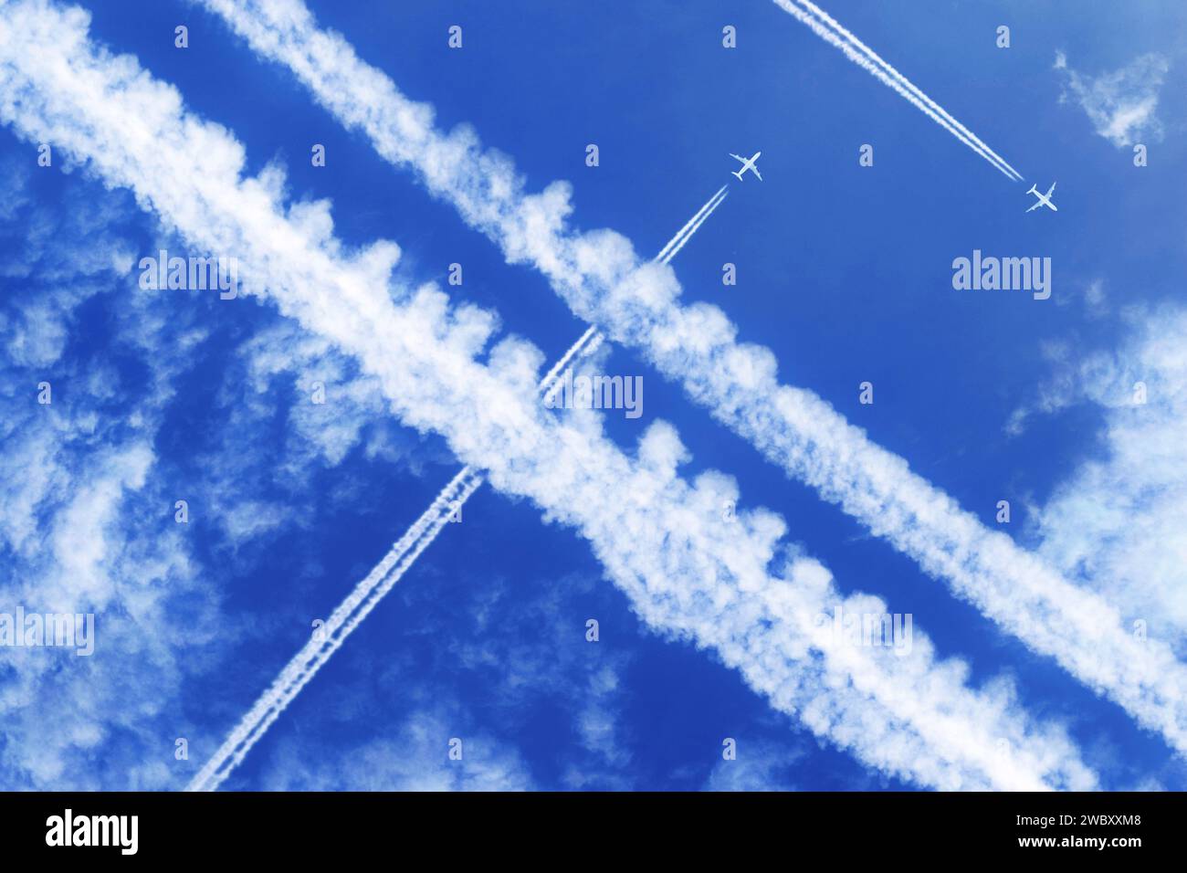 two airplanes with contrails high in the blue sky, crossing other ...