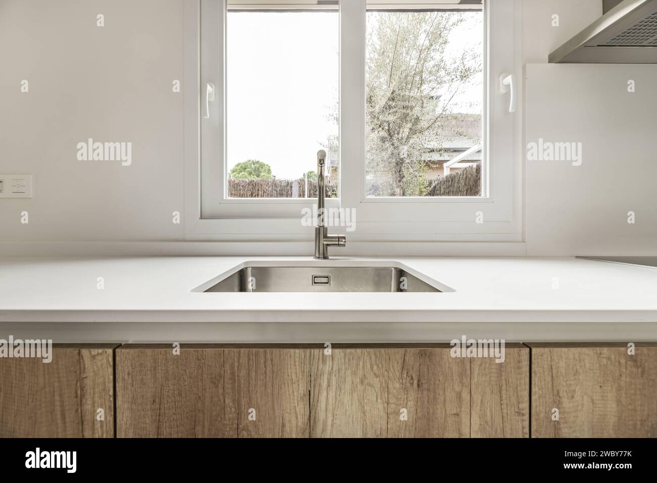 A small square sink in a kitchen with oak cabinets and white stone ...