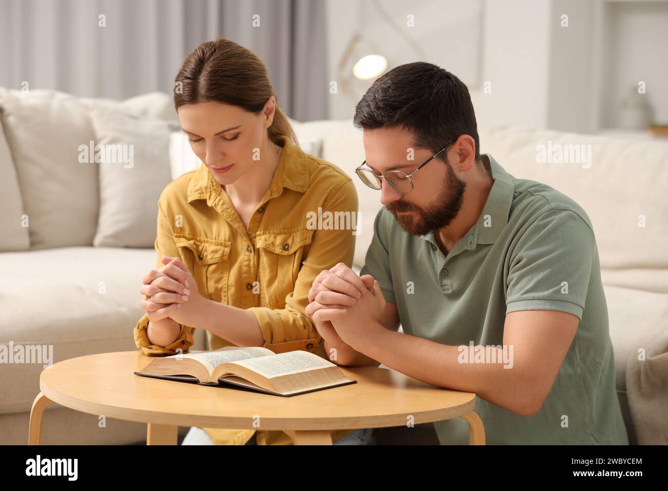 Family couple praying over Bible together at table indoors Stock Photo ...