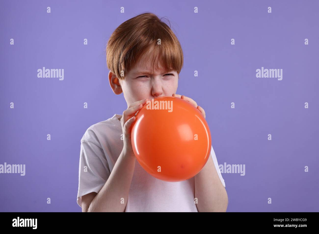 Boy inflating orange balloon on violet background Stock Photo - Alamy