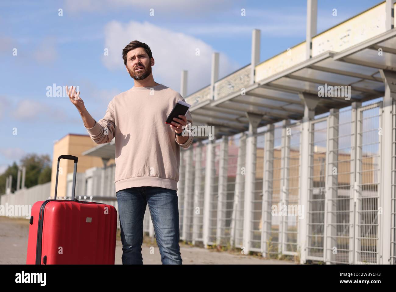 Being late. Worried man with red suitcase and passport outdoors, space ...