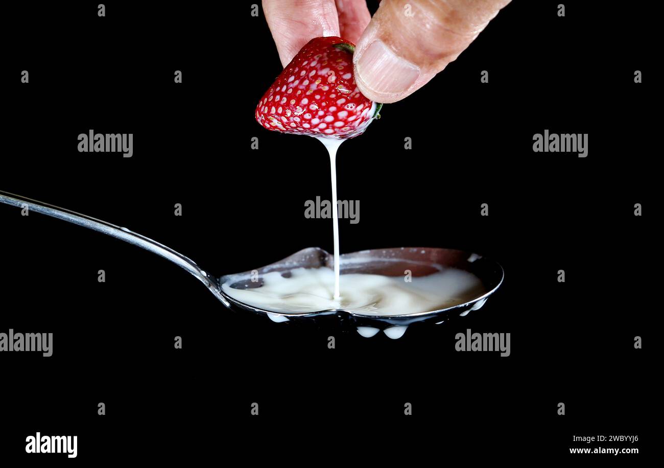 Fingers holding a strawberry dripping milk into a spoon Stock Photo - Alamy