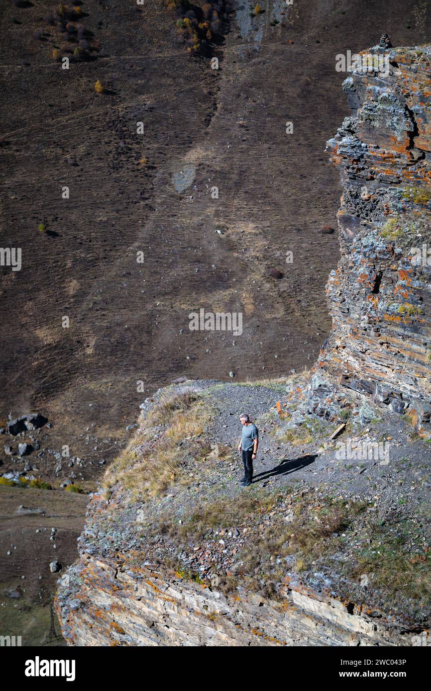 A man at the top of a mountain, standing majestically against a cliff ...