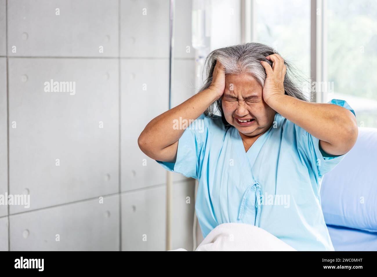 An elderly Asian woman having a severe headache, sitting in a hospital ...