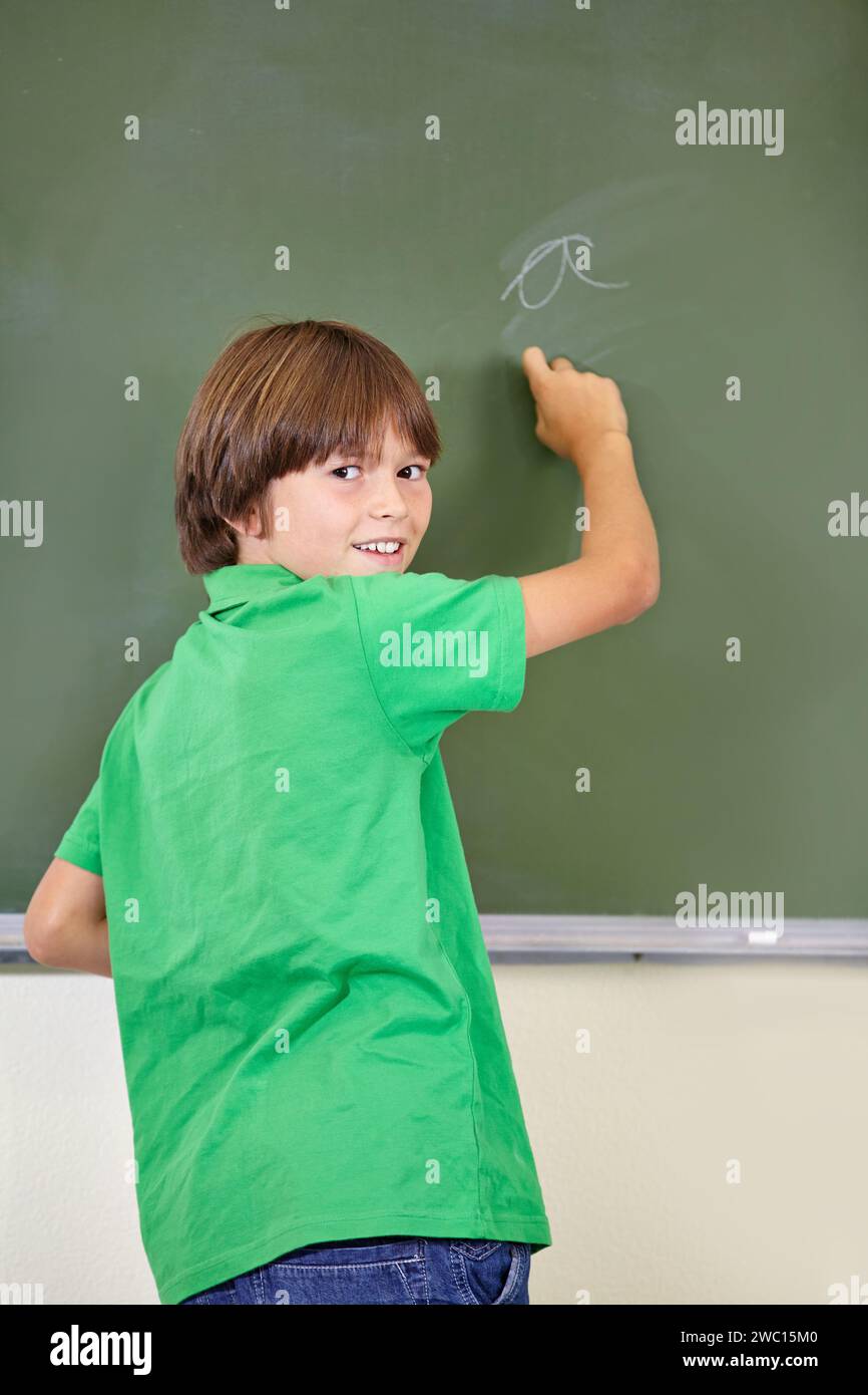 Portrait, smile and boy drawing on a chalkboard for child development ...