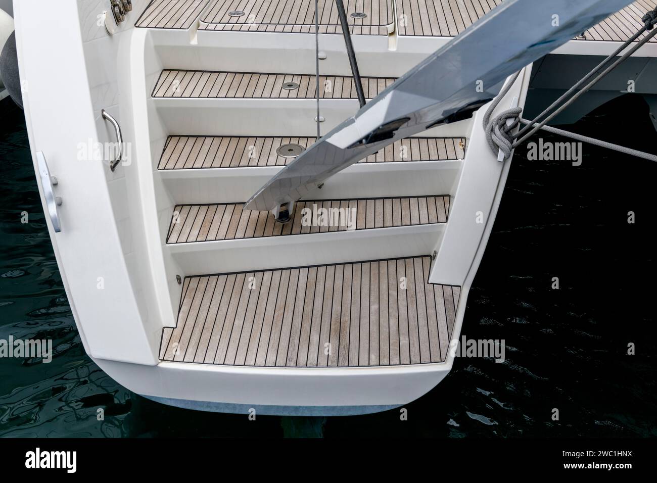 Stern of super luxury yacht berthed in marina. Teak deck on stern of sailing boat. Teak stairs ...