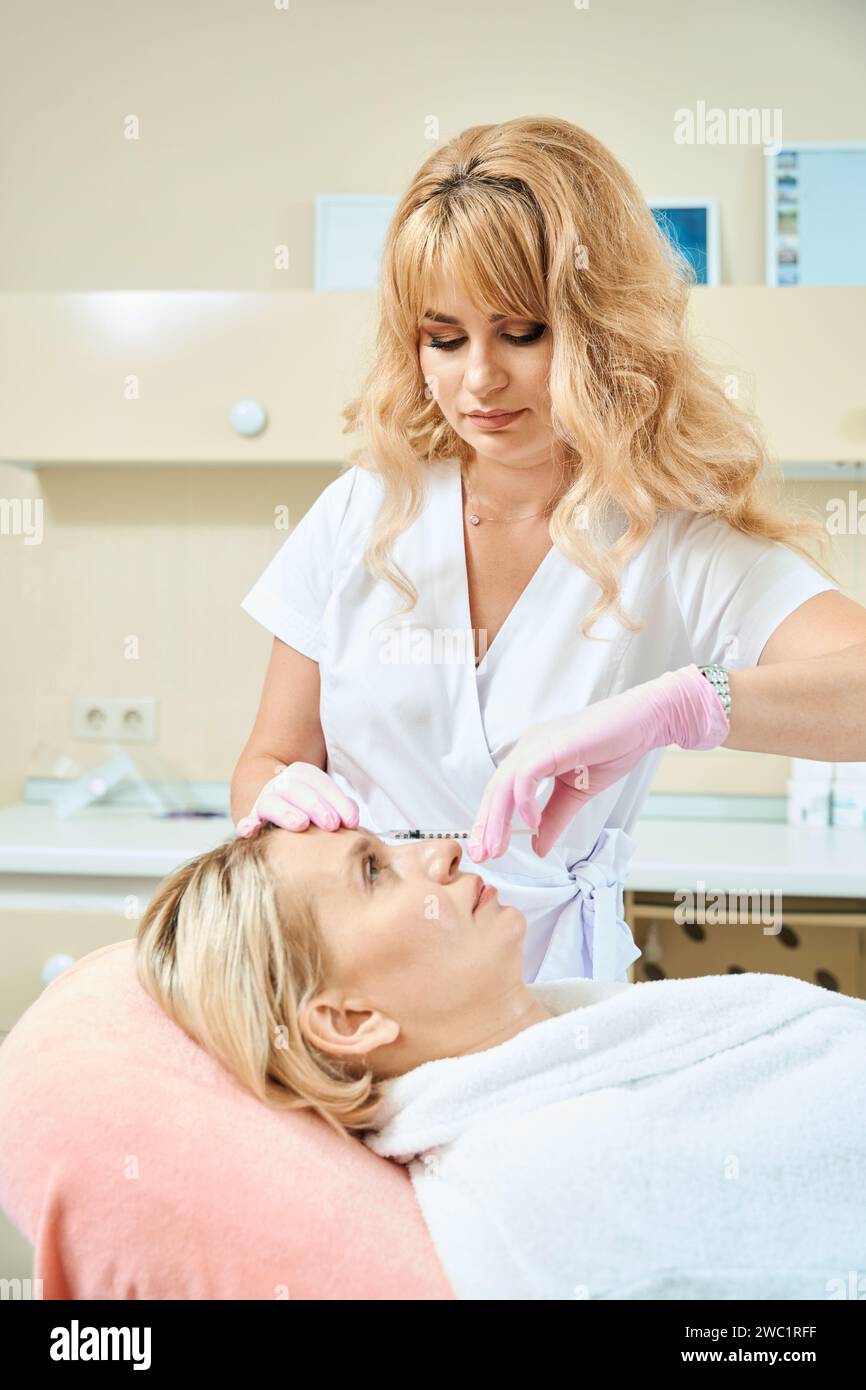 Female cosmetologist doing face beauty injection with syringe of woman ...