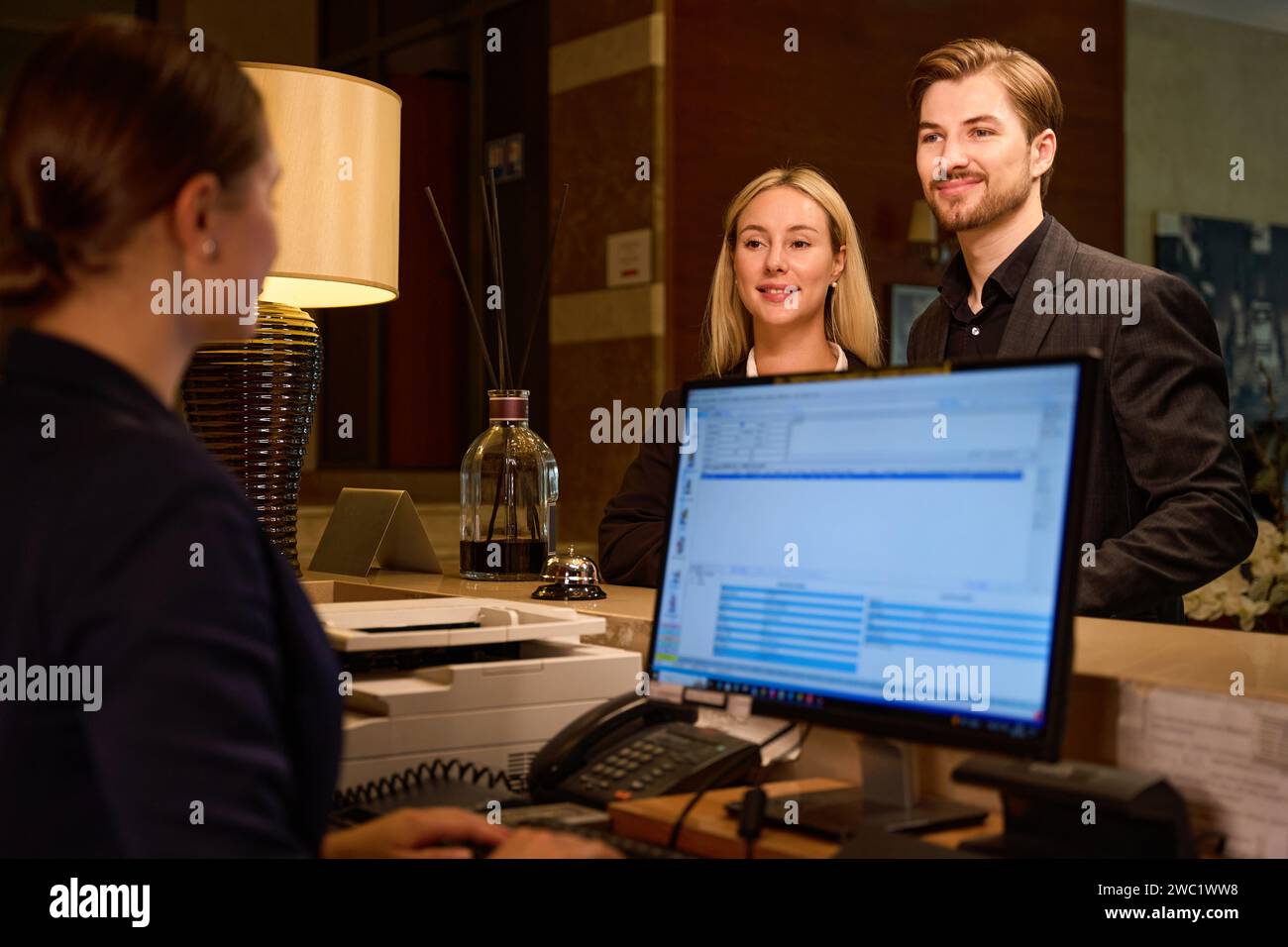 Receptionist typing on computer while couple standing at reception desk ...