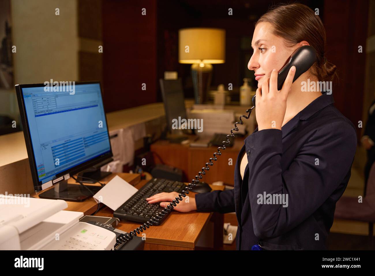 Side view photo of receptionist telephoning and typing on computer ...