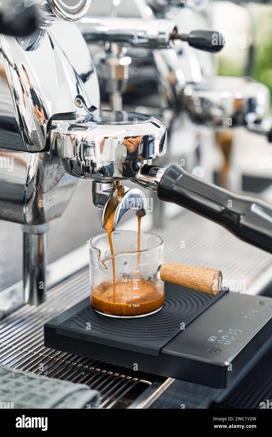Metallic espresso machine making hot coffee into dosing cup on counter ...