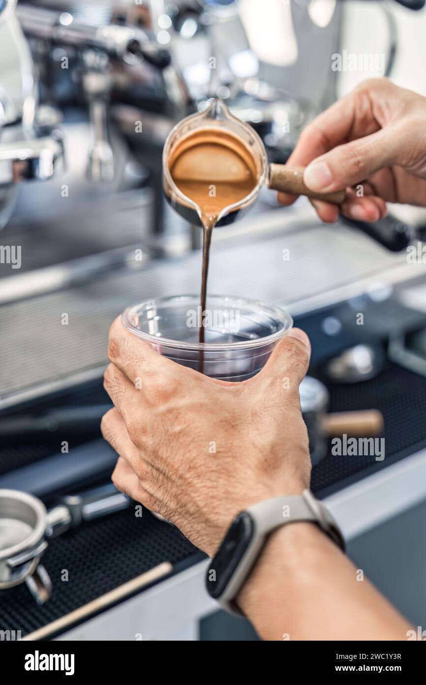 Barista pouring espresso coffee from dosing cup to plastic cup in ...