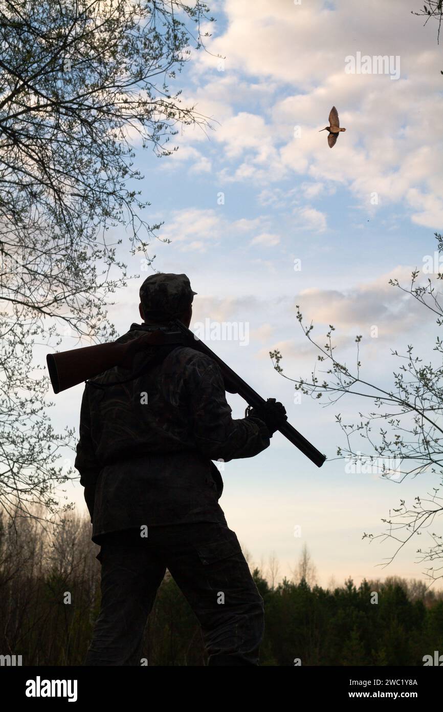 A hunter with an unloaded rifle on his shoulder stands in the twilight ...