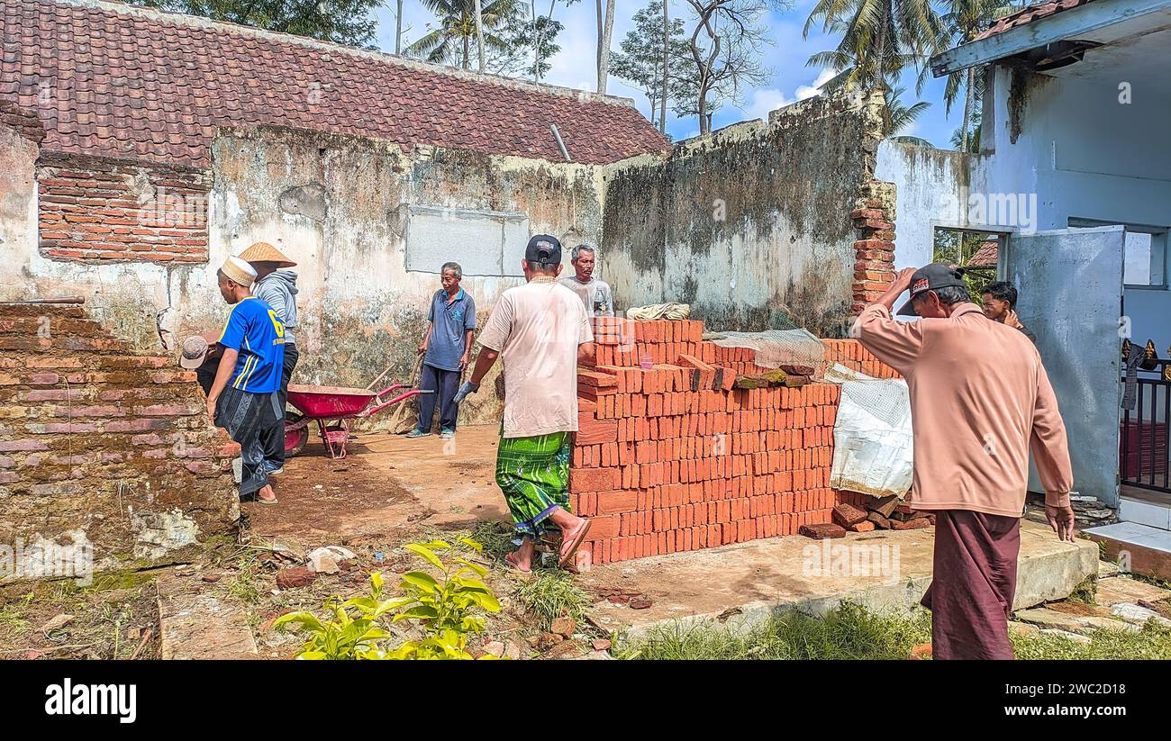 A group of men working together to lay red bricks on the wall of an old ...