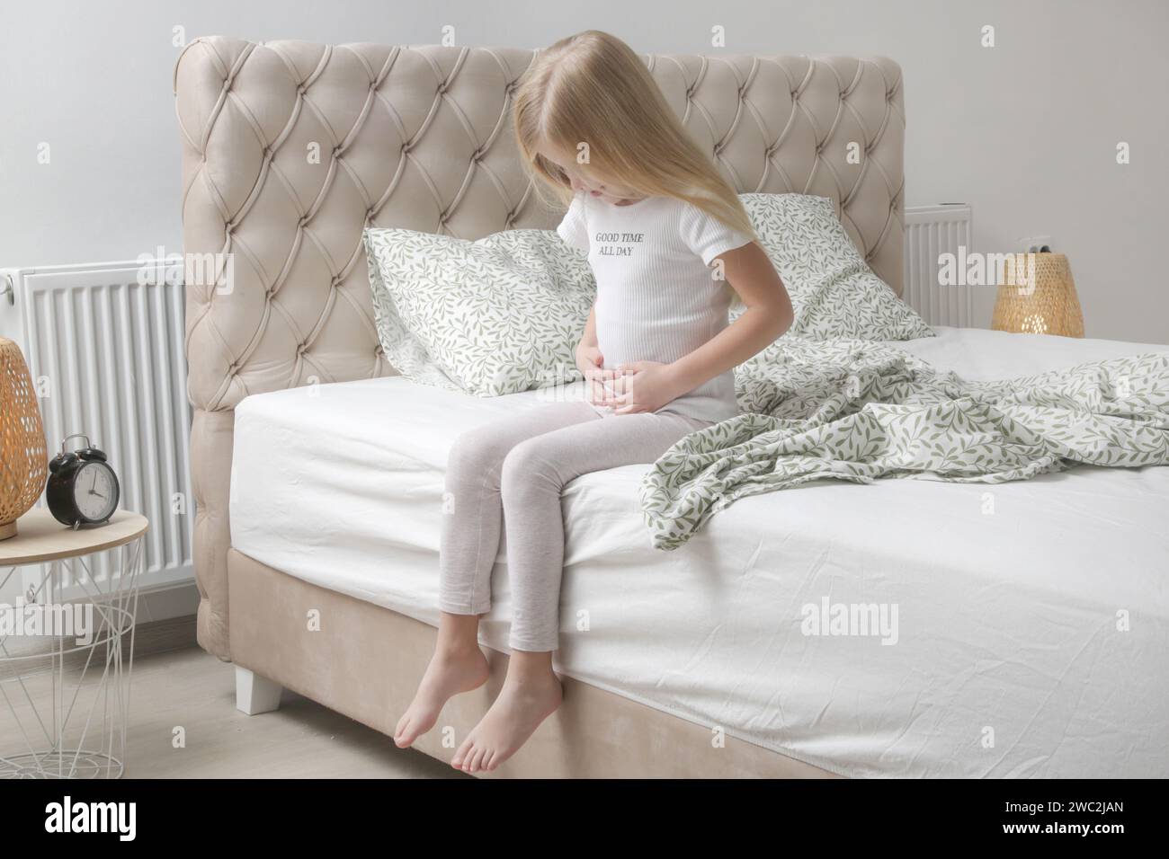 Little girl lying on bed in the bedroom with stomach pain. Hands on ...