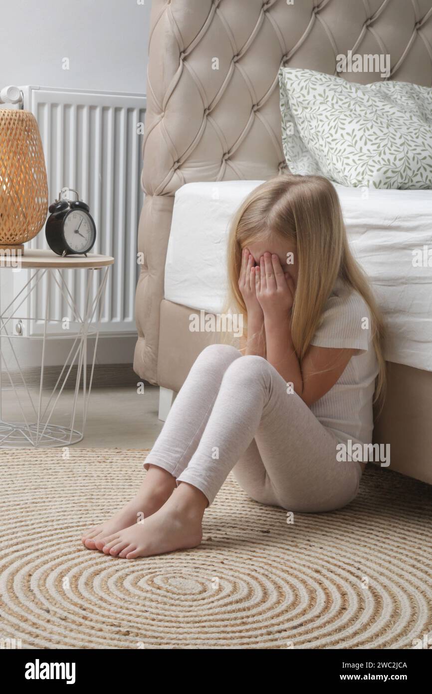 Little girl sitting in the bedroom, crying and covering face with hands ...