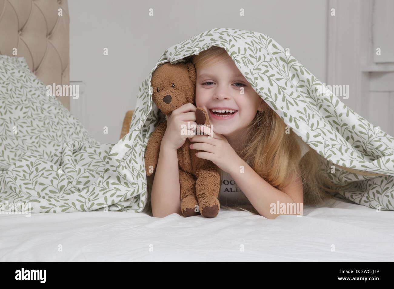 Adorable little preschool girl holding her teddy bear and hiding under ...
