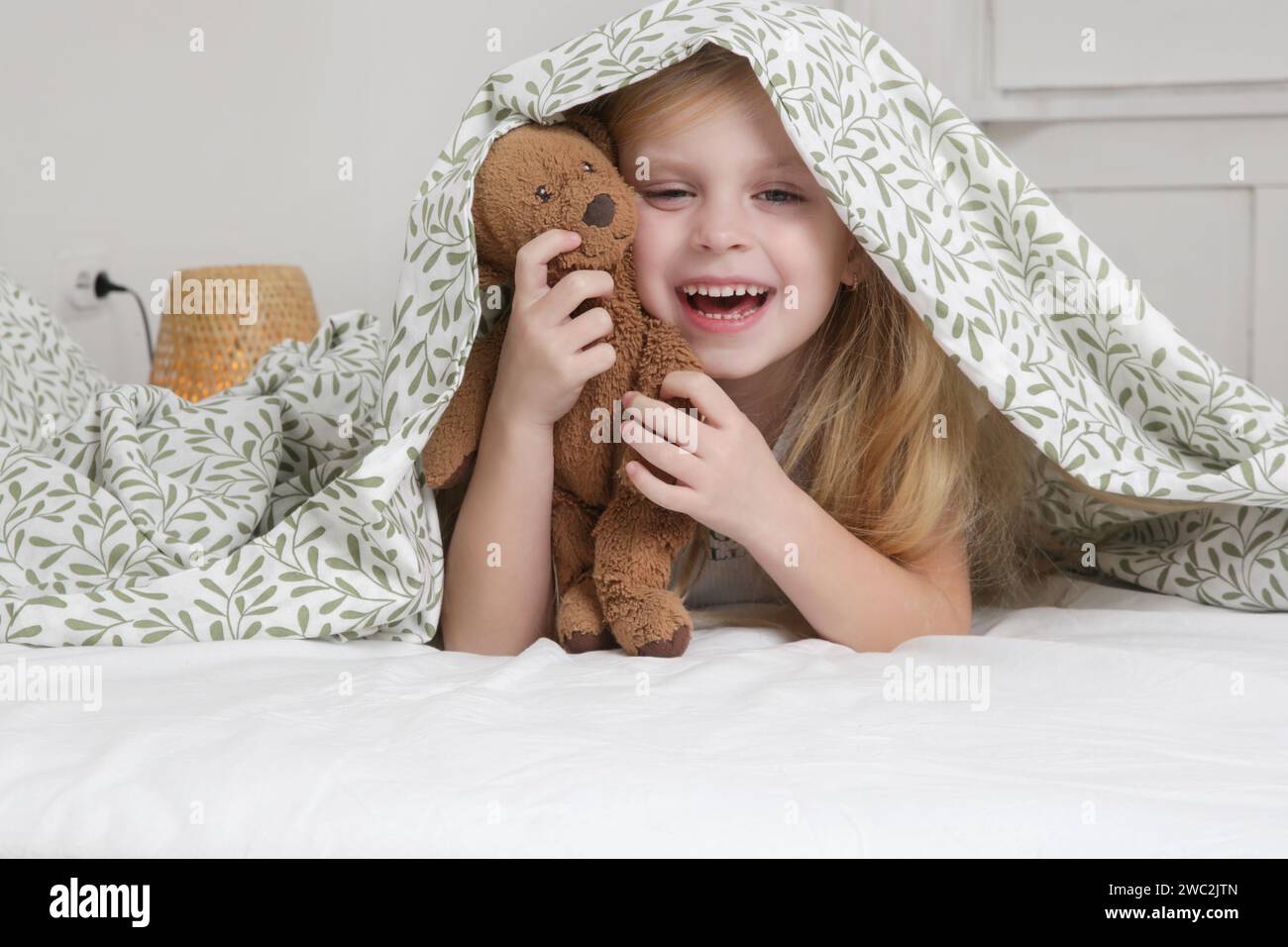 Adorable little preschool girl holding her teddy bear and hiding under ...