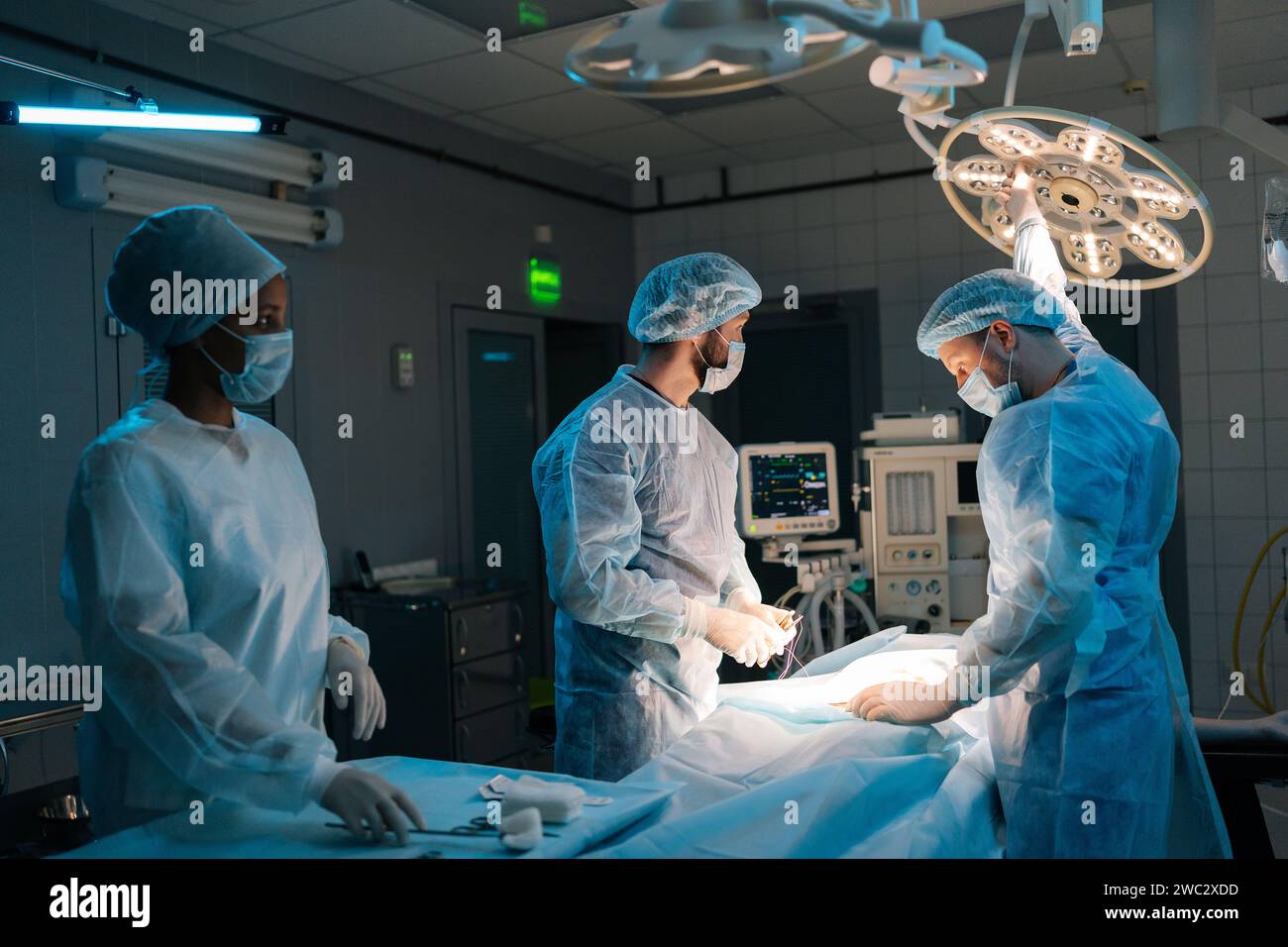 Male doctor in surgical uniforms and masks adjusting light before ...