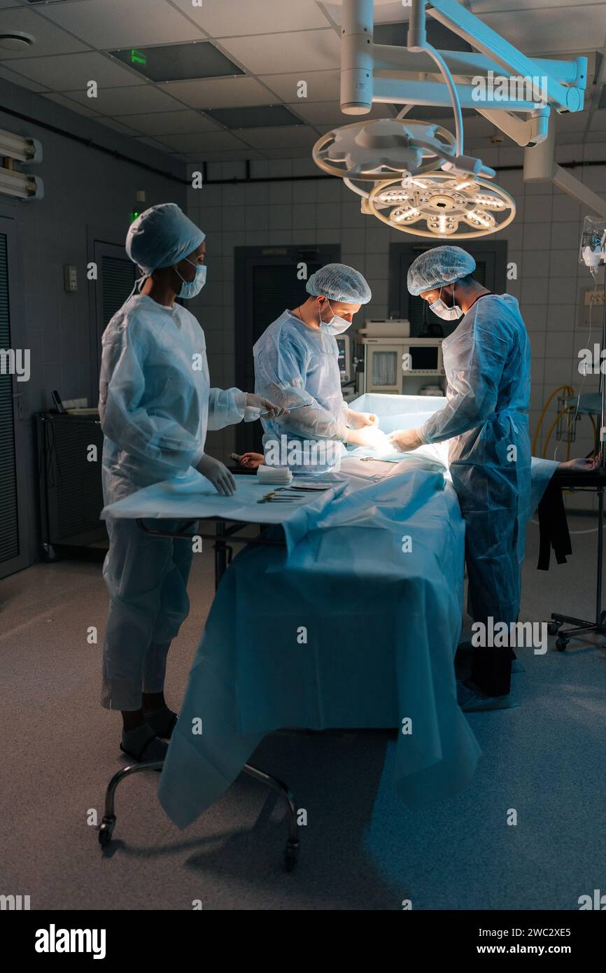 Vertical wide shot of two male surgeons assisted by African female ...