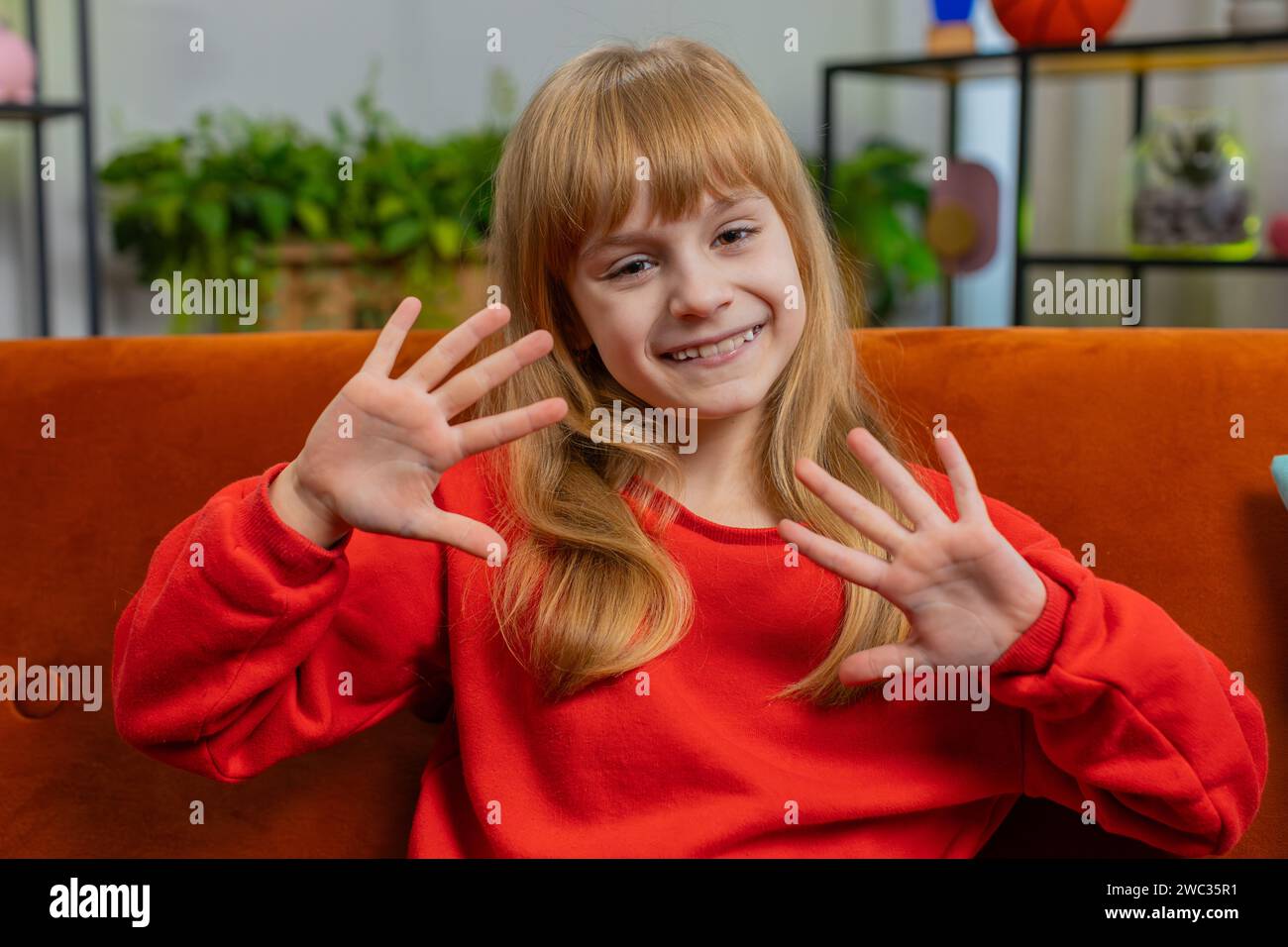 Young child girl smiling friendly at camera and waving hands gesturing ...