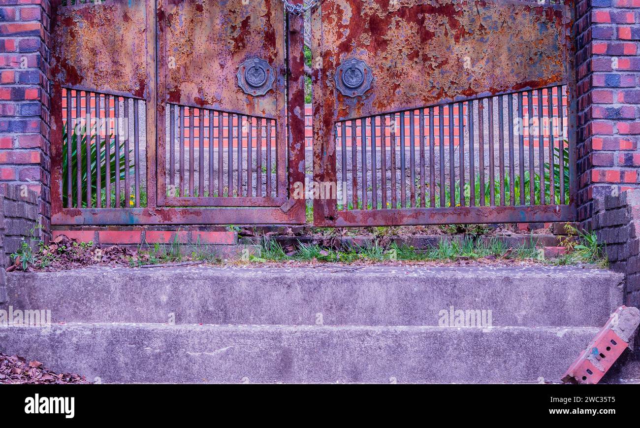 View of stairs leading to a chained rusted gate with red brick columns ...