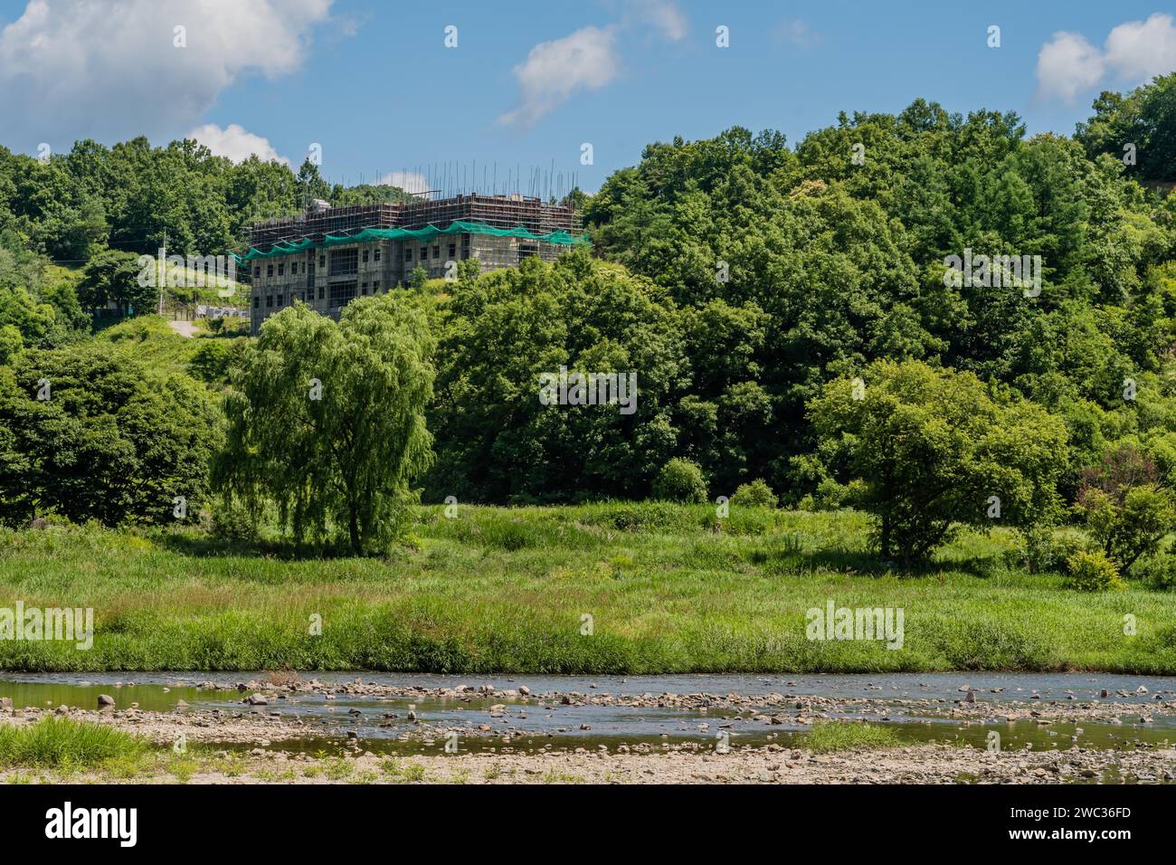 Concrete building under construction on top of tree covered hill with ...