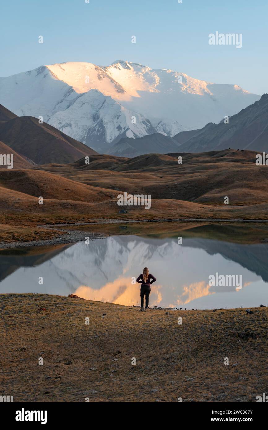 Hiker looking at mountain landscape, mountains reflected in a small ...