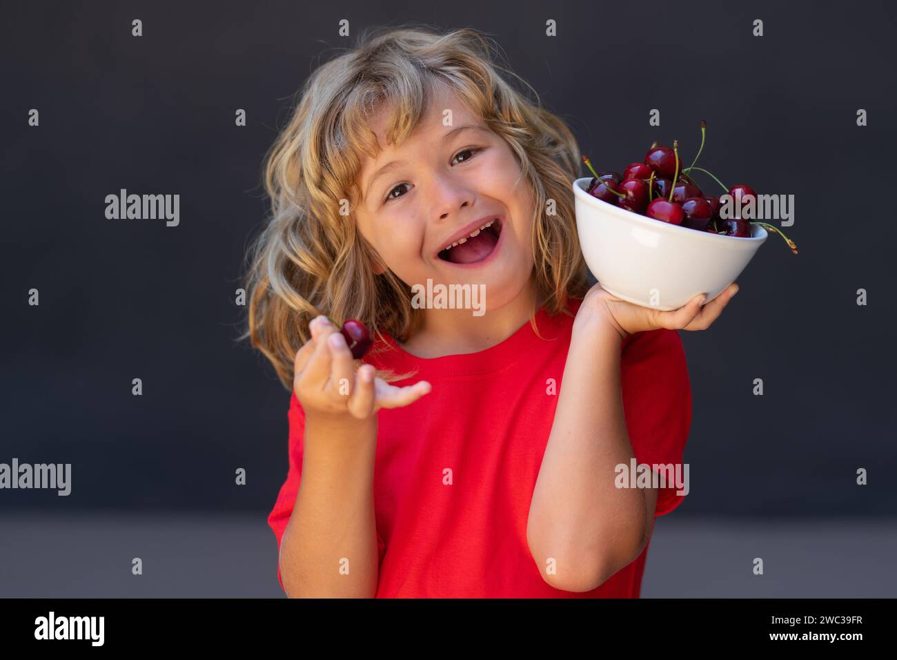 Cute little boy eating cherries, making funny faces and playing with ...